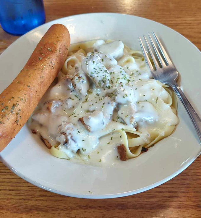 Fettuccine Alfredo with a breadstick standing at attention—comfort food that whispers "take a nap after this" with every creamy bite.