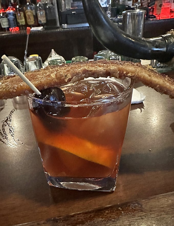 That's not just a Manhattan – it's a liquid amber time machine garnished with what appears to be bacon candy, because regular garnishes are for amateurs.