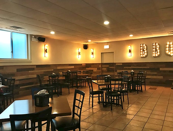 The second dining area feels like a modern saloon – warm lighting, wood-paneled walls, and those illuminated BBQ letters promising good things to come.