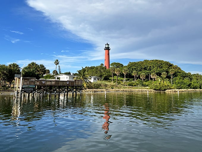 The lighthouse's reflection dances on the water like a crimson brushstroke on nature's canvas—Florida showing off again with minimal effort.