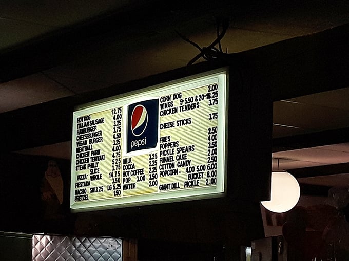 The illuminated menu board—a beacon of affordable indulgence where funnel cakes and pickle spears share equal billing with cinema classics.