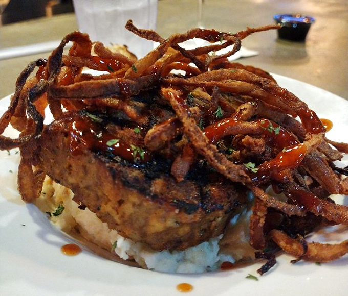 Meatloaf elevated to art form, topped with crispy onion straws and sitting on a cloud of mashed potatoes like a savory throne.