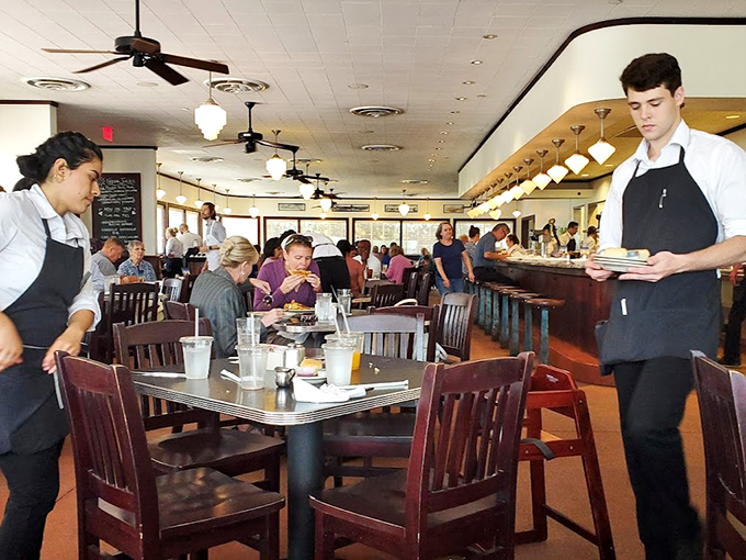 The dance of service in full swing—servers gliding between tables with plates of comfort food while diners lean into conversations worth having.