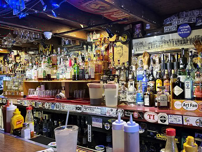 The bar isn't just stocked—it's an arsenal of liquid courage needed to face down The Thurmanator. Dollar bills and stickers mark the territory of past warriors.