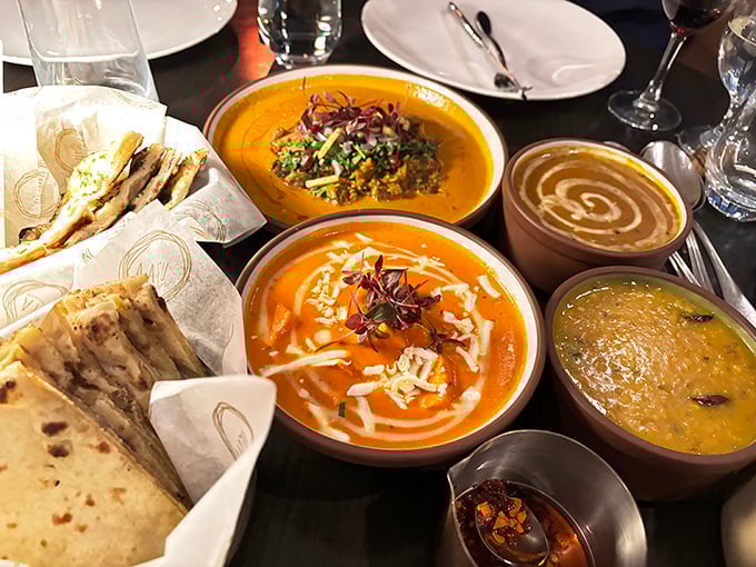 A table transformed into an artist's palette—golden curries swirled with cream, dal glowing like liquid sunshine, and naan ready to serve as the perfect edible spoon.