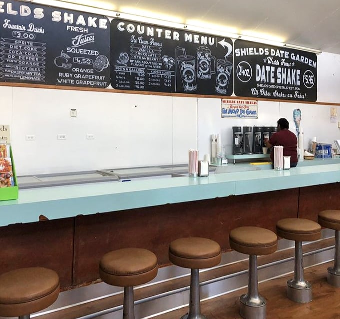 Classic counter seating beneath a chalkboard menu promises date shakes and fountain treats—a nostalgic nod to simpler, sweeter times.