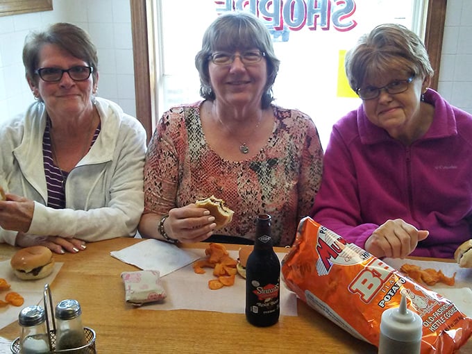 Three friends sharing smiles, burgers, and chips—the universal language of good food bringing people together since forever.
