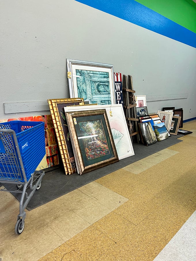 The wall of forgotten masterpieces. Gold frames and landscape prints lean casually, as if in an eccentric gallery's back room.