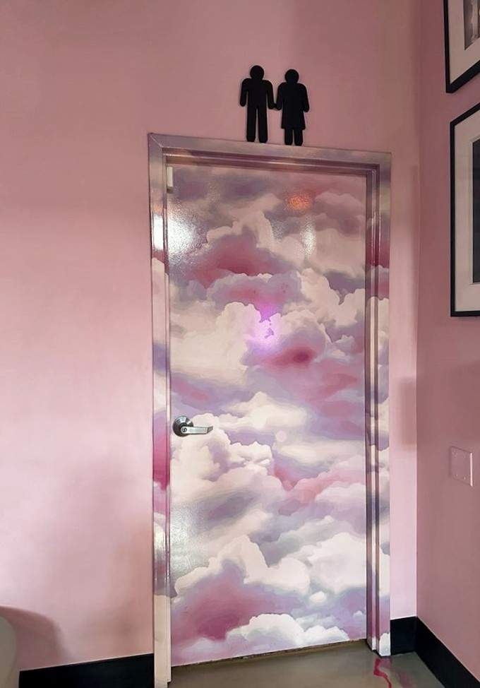 Even the restroom door transcends the ordinary—dreamy clouds painted in cotton candy hues promise a moment of zen in an unexpected place.