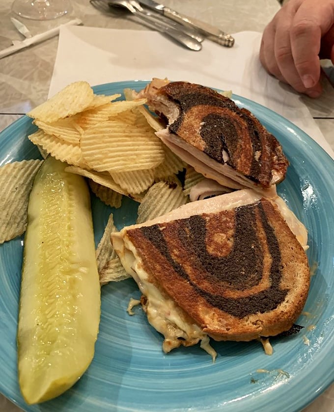 A perfectly grilled sandwich with the telltale marks of a panini press, accompanied by rippled chips and a pickle – comfort food that transcends time.