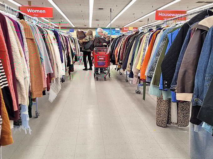 Serious shoppers navigate the clothing forest with practiced precision. The red cart means business—this isn't amateur hour in the thrift shopping leagues.