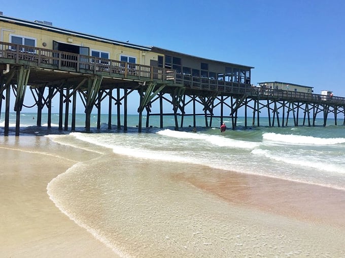 Engineering marvel! Crabby Joe's pier stretches dramatically over the Atlantic waves, creating the ultimate "dinner and a show" as surfers ride below.