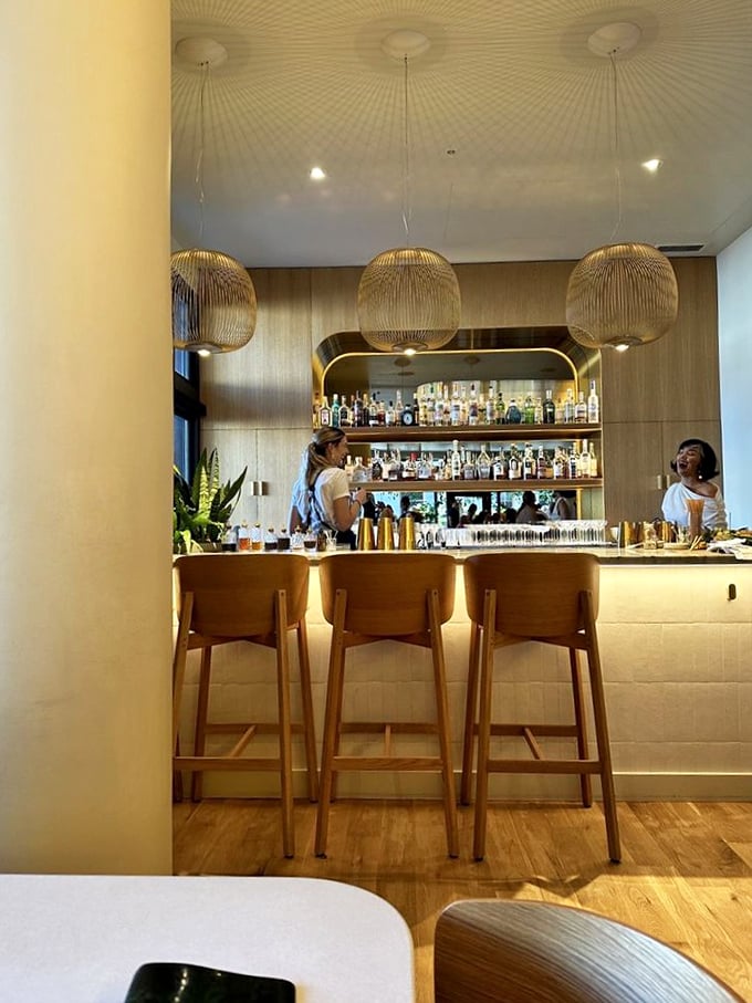 The bar at Kann doesn't just serve drinks—it creates liquid companions for your culinary journey. Golden pendant lights cast a spell of conviviality.