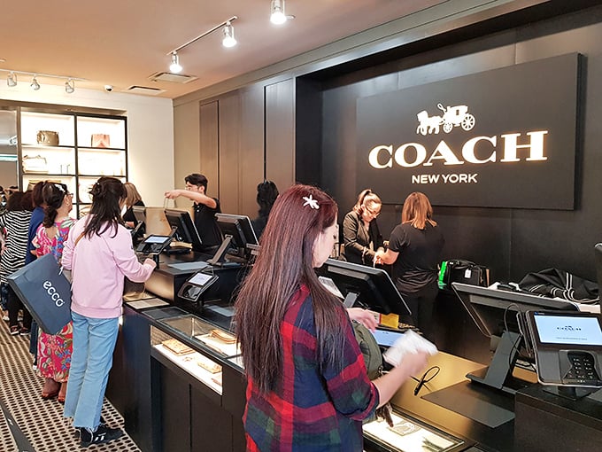 The Coach checkout counter—where credit cards come to sacrifice themselves on the altar of luxury goods at surprisingly reasonable prices.