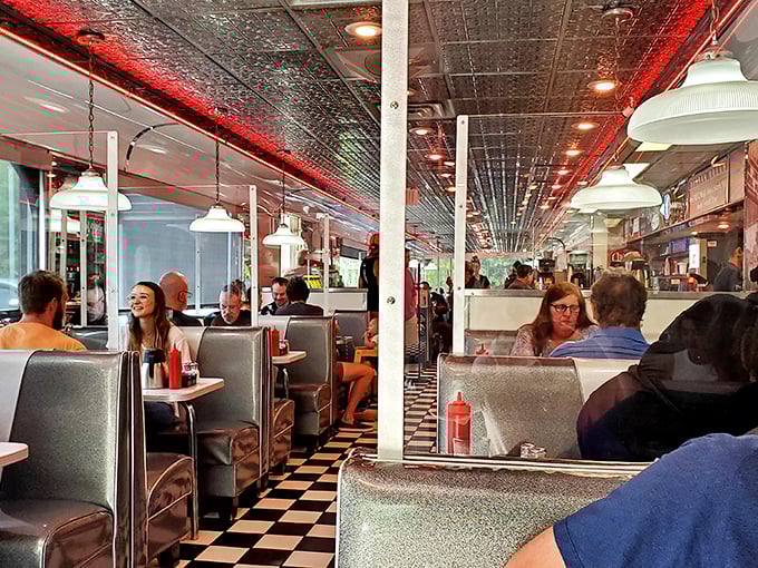 The classic booth seating creates little islands of conversation, where strangers become neighbors under the warm red glow of ceiling lights.