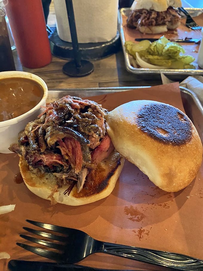 The pulled pork sandwich—where bread becomes merely a delivery system for smoky, juicy perfection. Napkins required, restraint impossible.