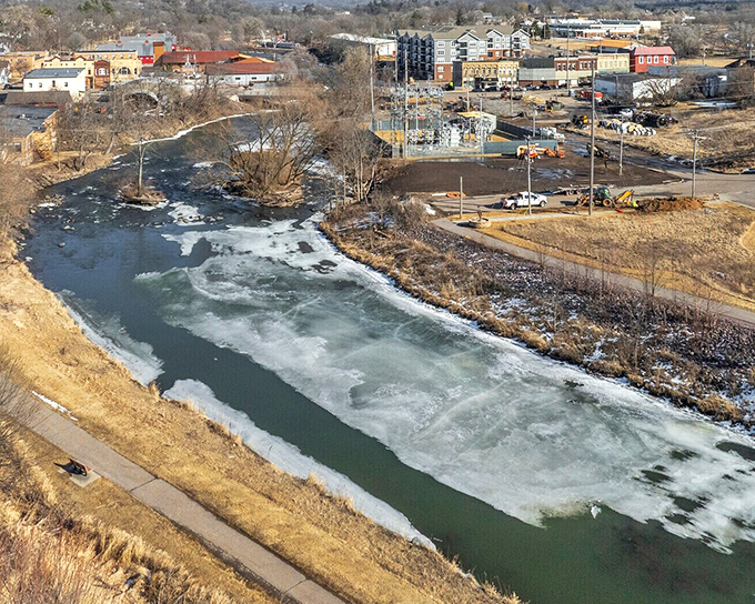 The Baraboo River, partially frozen in winter's grip, creates a stunning natural boundary between the town and its commercial developments.