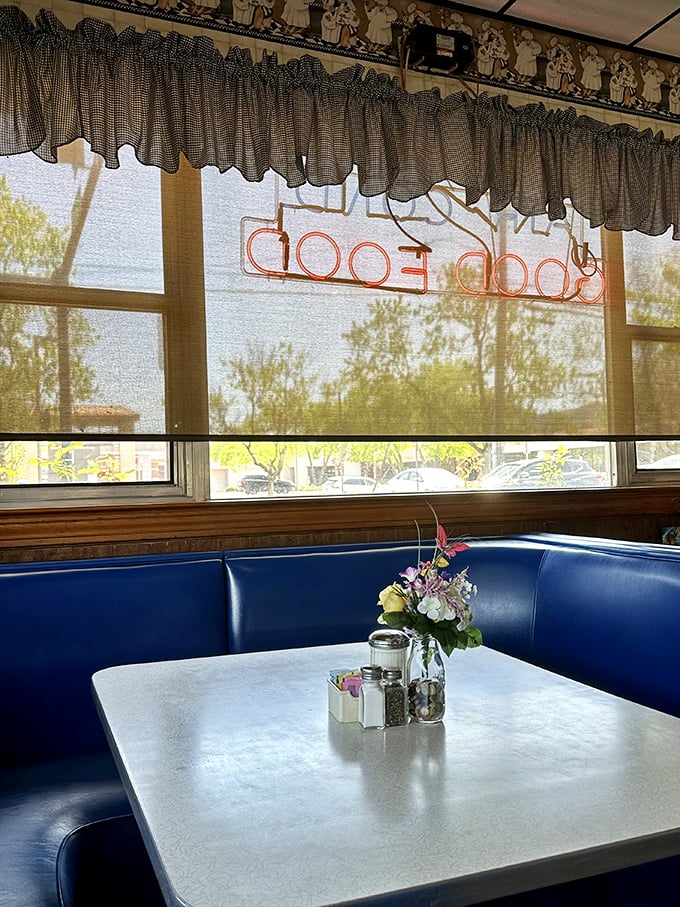 Blue booth seating bathed in morning light, with flowers and salt and pepper standing ready. The stage is set for breakfast theater—you're just waiting for your starring role.