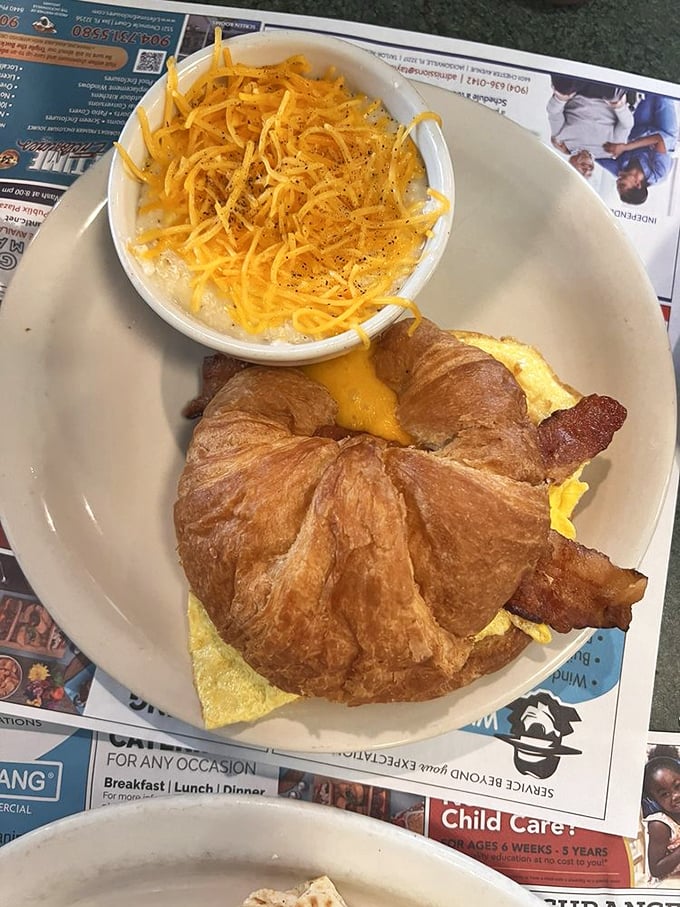 Breakfast sandwich architecture at its finest – a golden croissant cradling eggs, bacon and cheese with a side of cheesy grits for good measure.