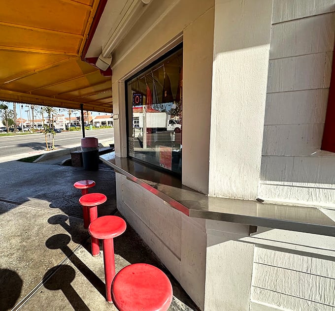 Red stools lined up like loyal soldiers awaiting your command. The counter service window—where magic happens with minimal fanfare.