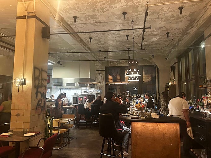 The dining room buzzes with conversation and clinking glasses—industrial-chic meets warm hospitality under weathered ceilings that tell stories of the building's past.