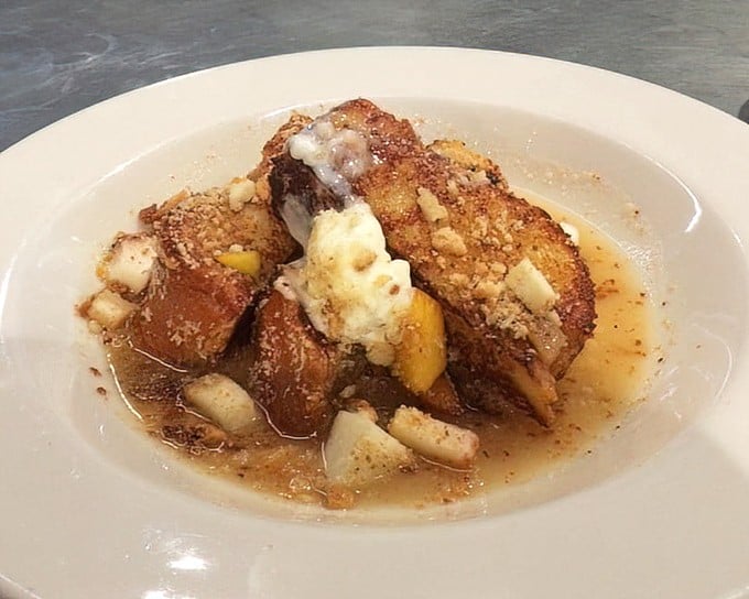 French toast that transcends ordinary breakfast boundaries. Golden-brown challah soaking in sweet syrup with fresh fruit standing by—morning decadence at its finest.