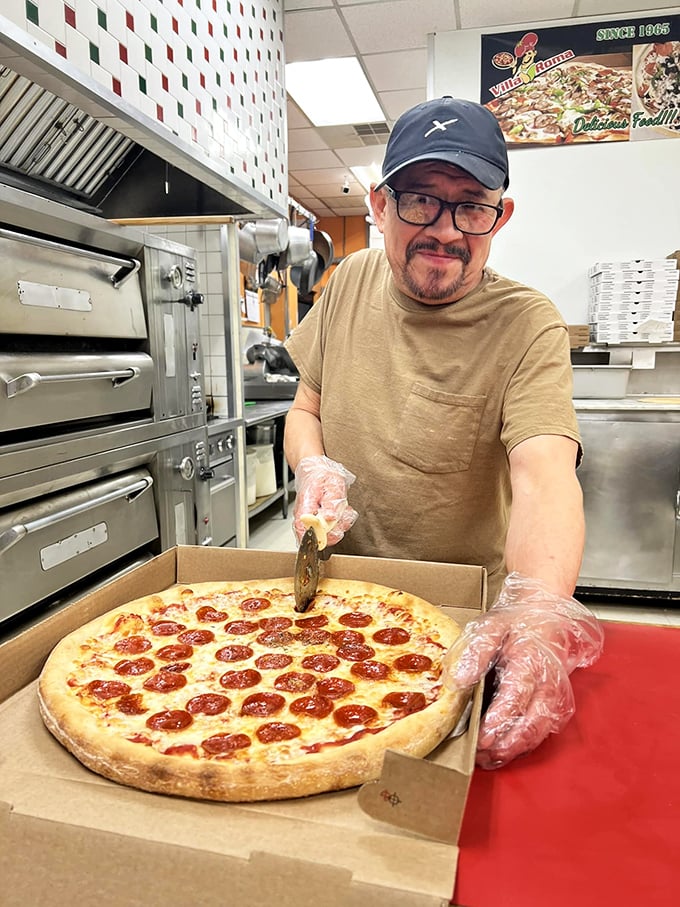The pizza maestro at work – where every pepperoni placement is deliberate and years of experience show in each confident slice of the cutter.