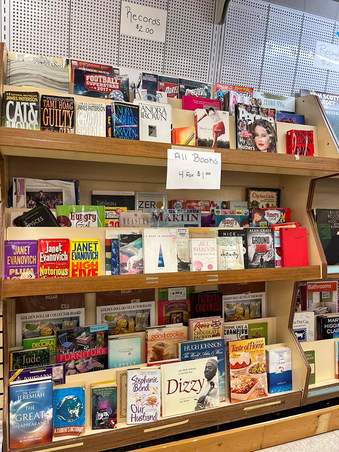 Literary treasures at four for a dollar – Janet Evanovich mysteries stacked alongside cookbooks and biographies. Bibliophile heaven at bargain prices.