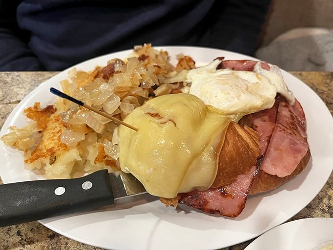 Breakfast architecture at its finest – layers of ham, egg, and cheese on a croissant with home fries standing guard nearby.