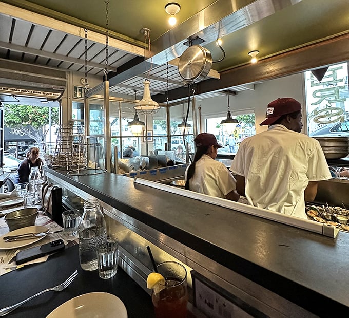 The open kitchen reveals the choreographed dance of professional seafood preparation. Nothing builds confidence like watching your oysters being shucked with precision.