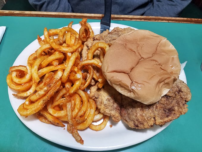 A pork tenderloin sandwich that's having an identity crisis—it thinks it's bigger than its bun. Those curly fries are practically doing gymnastics.
