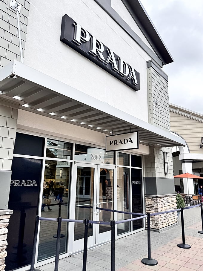 Prada's sleek storefront promises luxury at less painful prices. That velvet rope isn't just for show—it's there to create the illusion of exclusivity in a land of discounts.