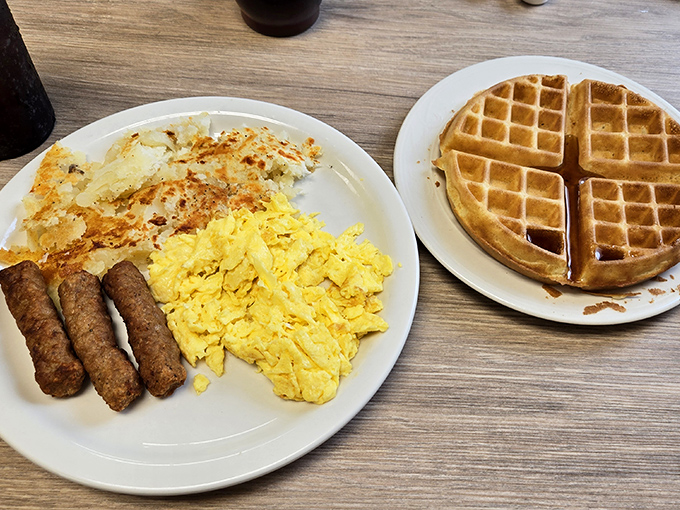 A breakfast trinity that would make any morning better—golden waffle, scrambled eggs, and sausage links that snap with that perfect first bite.
