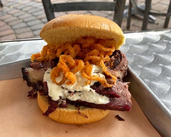 This sandwich defies gravity and good manners – stacked high with smoked meat, creamy topping, and crispy onions. A beautiful mess worth every napkin.