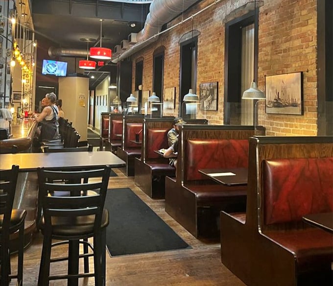 Cozy booths line the exposed brick walls, creating intimate dining nooks. Industrial meets comfort in this thoughtfully designed space.