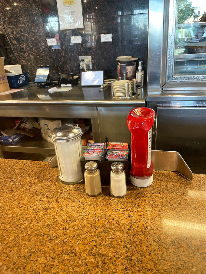 Those classic diner condiments—salt, pepper, and ketchup—standing at attention, ready to enhance whatever comfort food masterpiece arrives at your table.