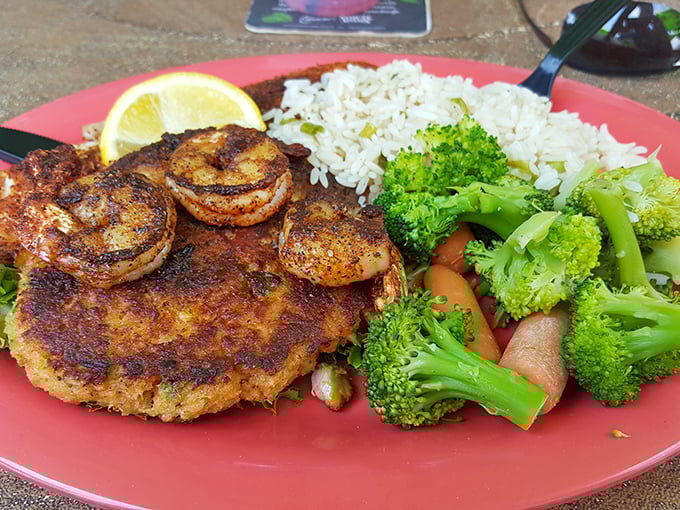 This crab cake doesn't just sit on the plate—it commands attention, flanked by perfectly blackened shrimp and colorful vegetables.