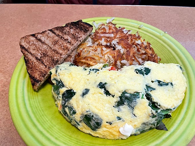 This isn't just an omelet—it's a fluffy yellow canvas painted with vibrant spinach, served alongside crispy hash browns and hearty toast.