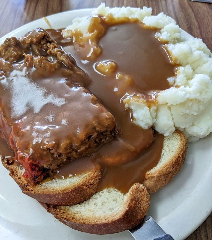 Open-faced meatloaf sandwich swimming in gravy—comfort food that doesn't need a therapist's license. That mashed potato dam holding back the gravy river deserves an engineering award.