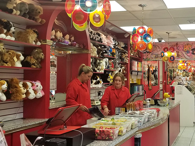 The red-coated candy specialists – modern-day Willy Wonkas orchestrating sweet symphonies behind gleaming glass. Their job satisfaction is visible.