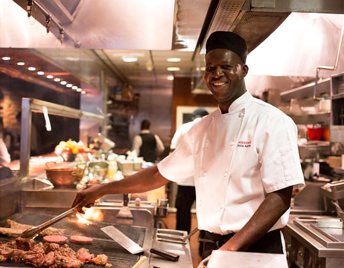 The smile says it all—this chef knows he's about to make your day significantly better with whatever's sizzling on that grill.
