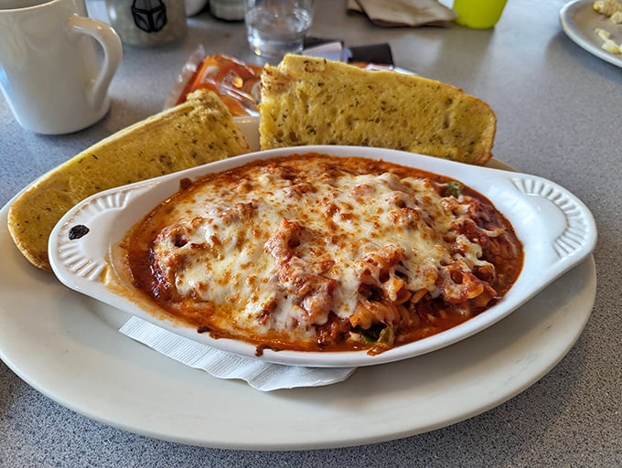 Melted cheese forms a golden canopy over this baked pasta dish, while garlic bread waits patiently for its supporting role in sauce management.