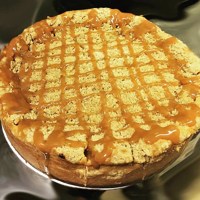 Caramel drizzled with mathematical precision across a cheesecake that looks dense enough to have its own gravitational pull. Diet plans enter at their own risk.
