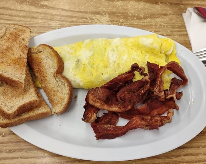 The classic American breakfast plate: fluffy omelet, crispy bacon, and toast waiting for its butter bath. Simple pleasures are often the most profound.