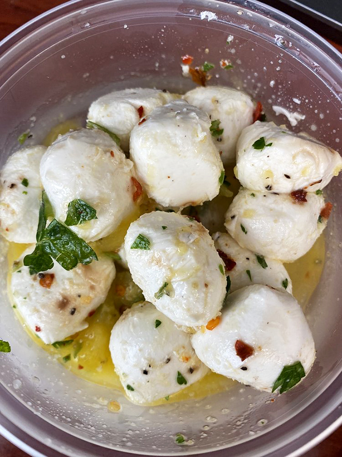 Fresh mozzarella balls bathing in herbed olive oil—little orbs of dairy perfection that might not make it home before being devoured.