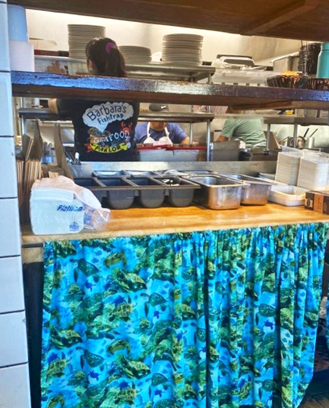Behind the scenes where the magic happens—staff in the open kitchen preparing ocean treasures. That blue fish-patterned curtain is the culinary equivalent of a superhero's cape.