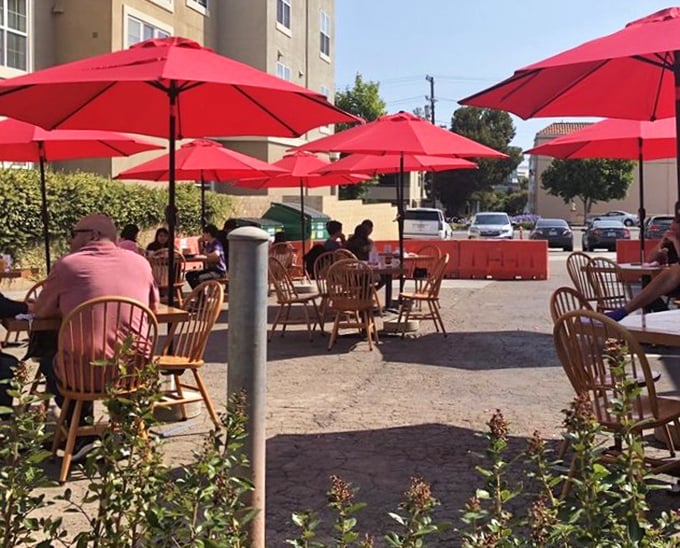 Outdoor dining under cherry-red umbrellas – California sunshine and pancakes proving that some combinations are simply unbeatable.