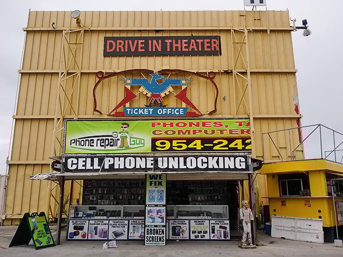 The drive-in theater entrance stands as a monument to entertainment eras past, now sharing space with modern cell phone repair services.