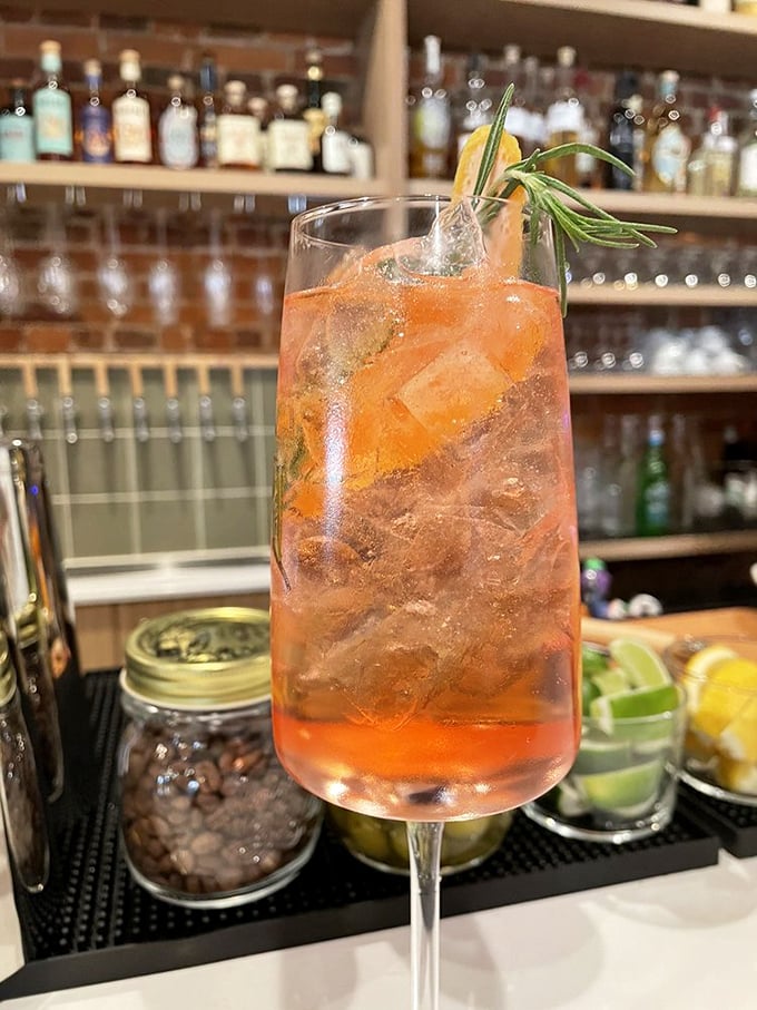 The Riverside Spritz glows amber in evening light, rosemary sprig standing tall like a tiny aromatic flagpole.