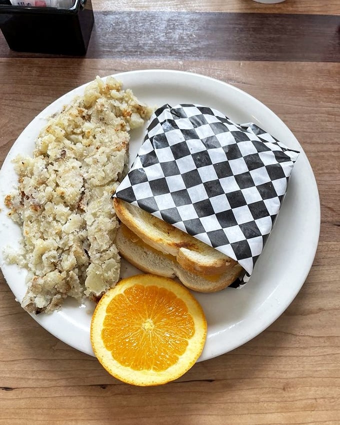 The perfect partnership – a sandwich wrapped in checkered paper alongside hash browns and a bright orange slice for a pop of color.
